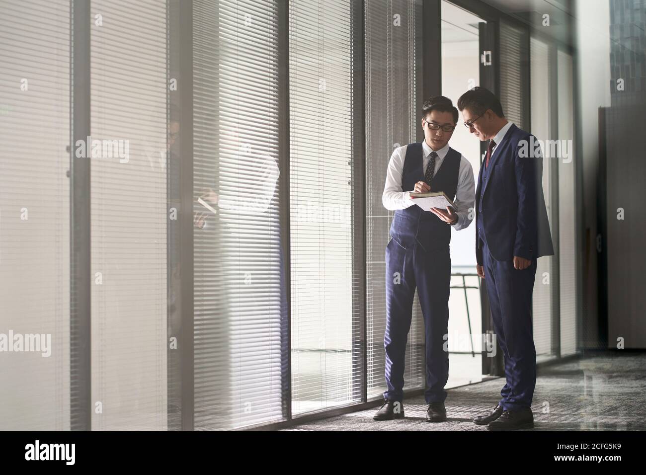 two asian corporate executives standing in office discussing business ...