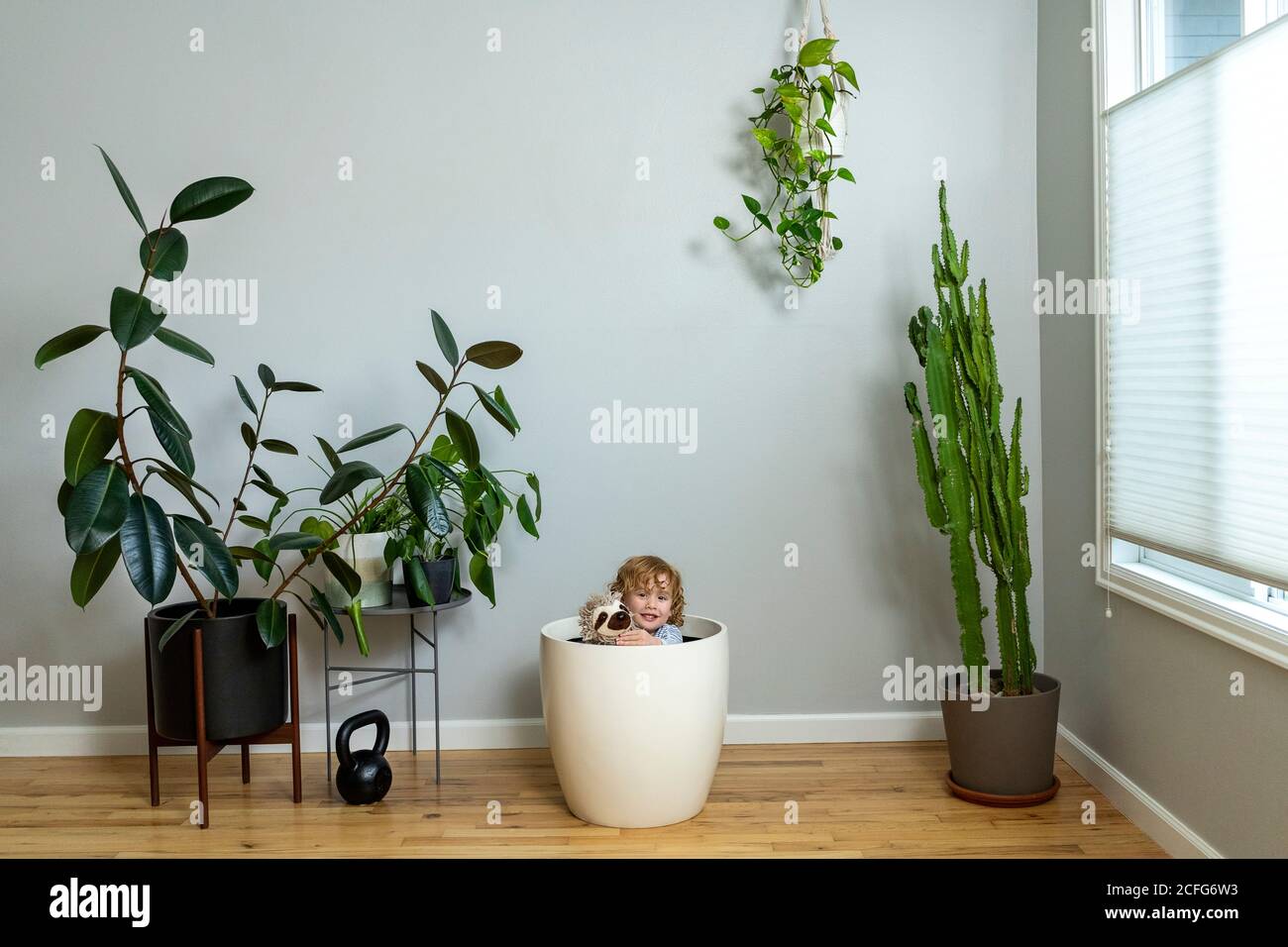 Smiling young child snuggles a stuffed toy sloth while sitting inside ...
