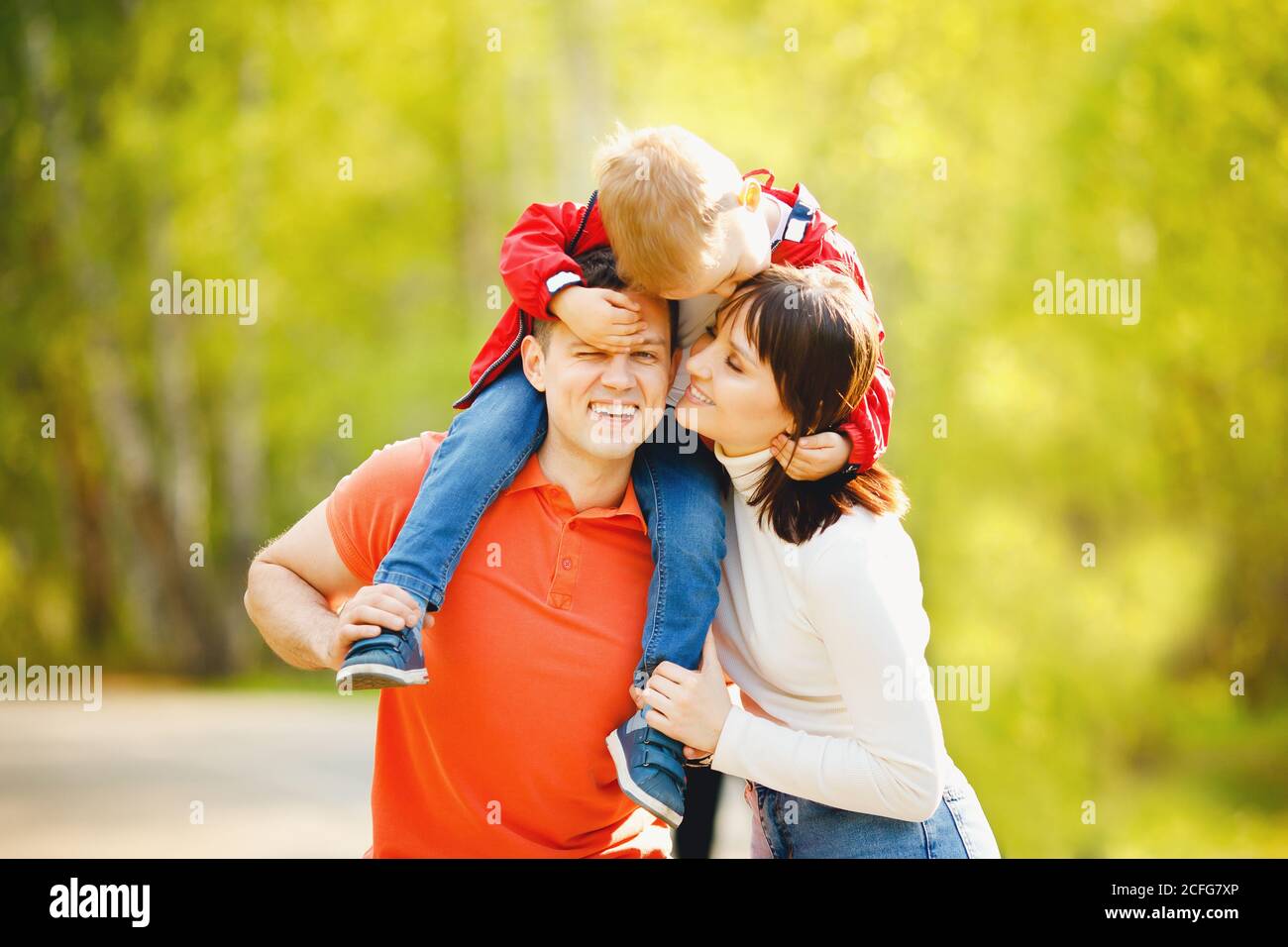 Boy smiles and hugs happy parents, sits on his father neck. Family walk ...