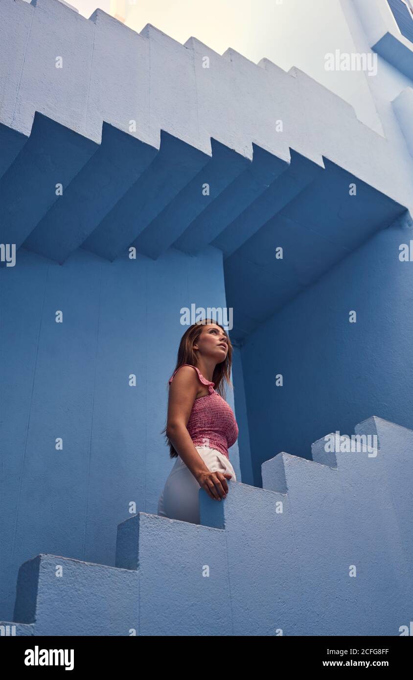 Side view of Woman walking upstairs on modern blue building looking up ...