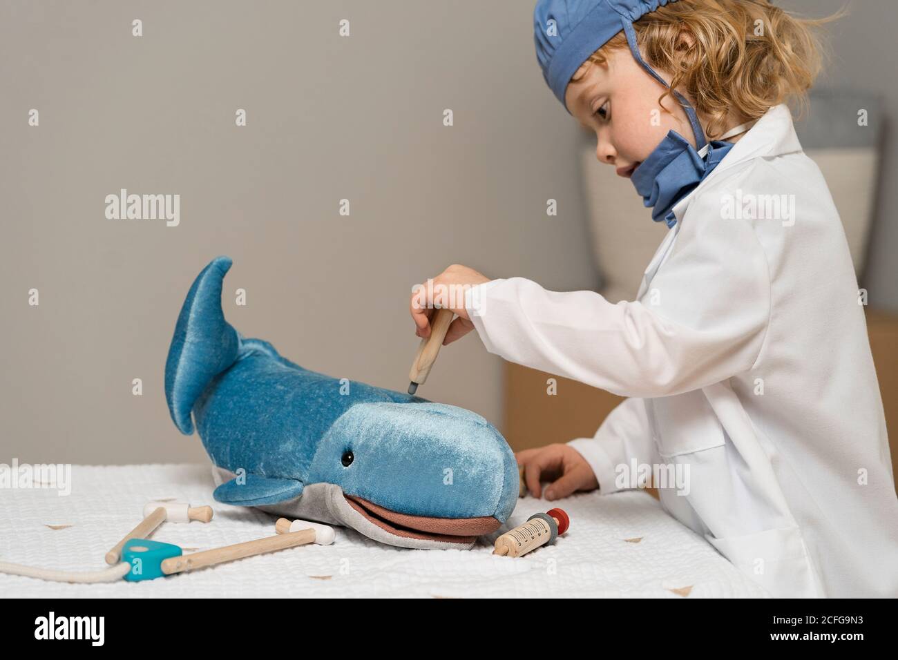 young child wearing medical PPE examines a plush toy whale by taking ...