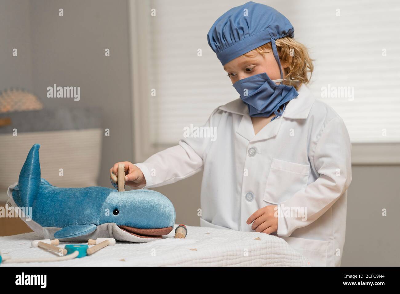 young child wearing medical PPE examines a plush toy whale by taking ...