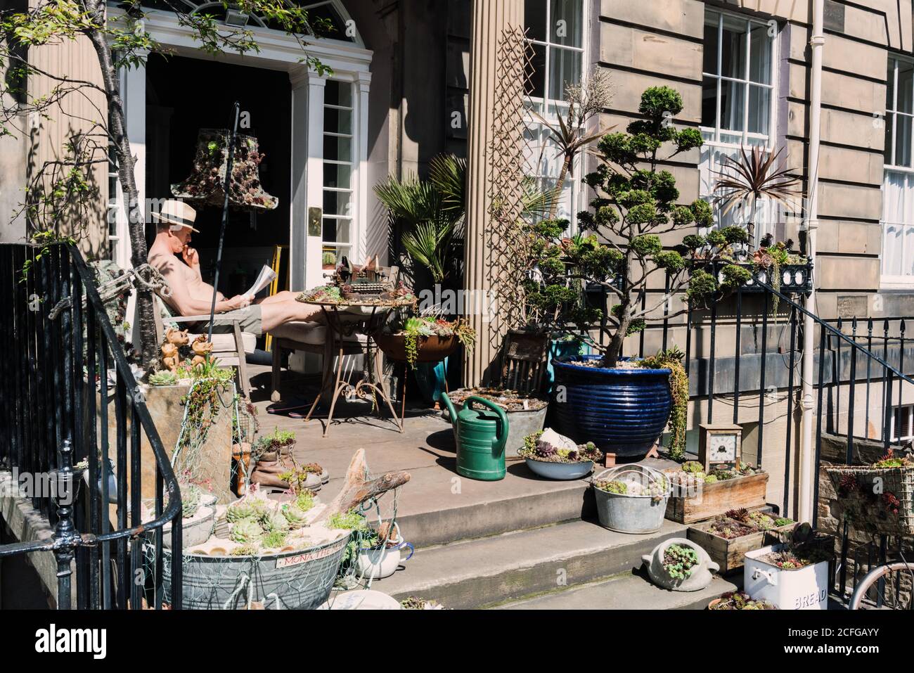 man reading newspaper on porch with creative plants and trees in boxes ...