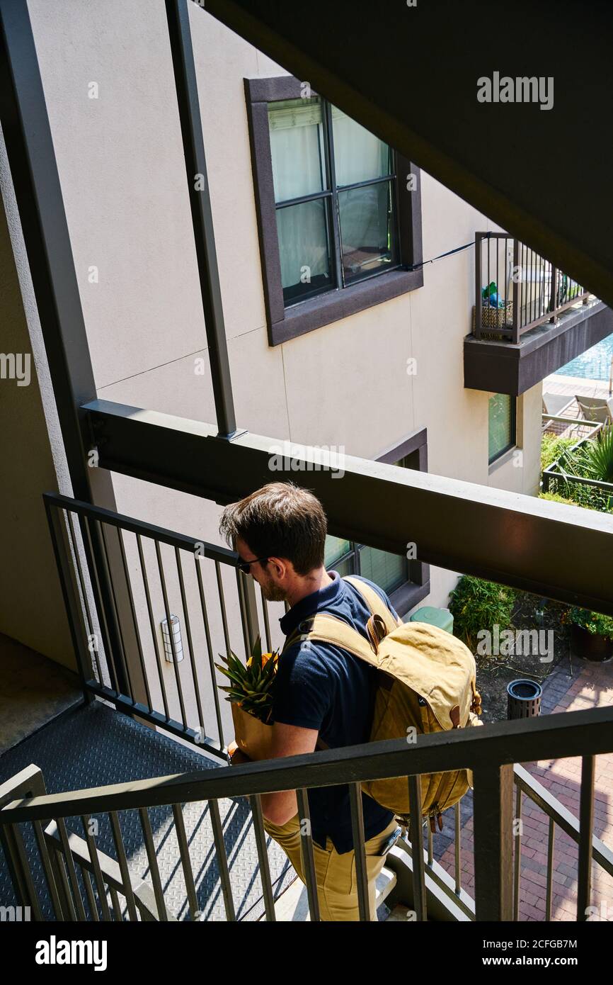 From above back view of male with paper bags and backpack walking ...