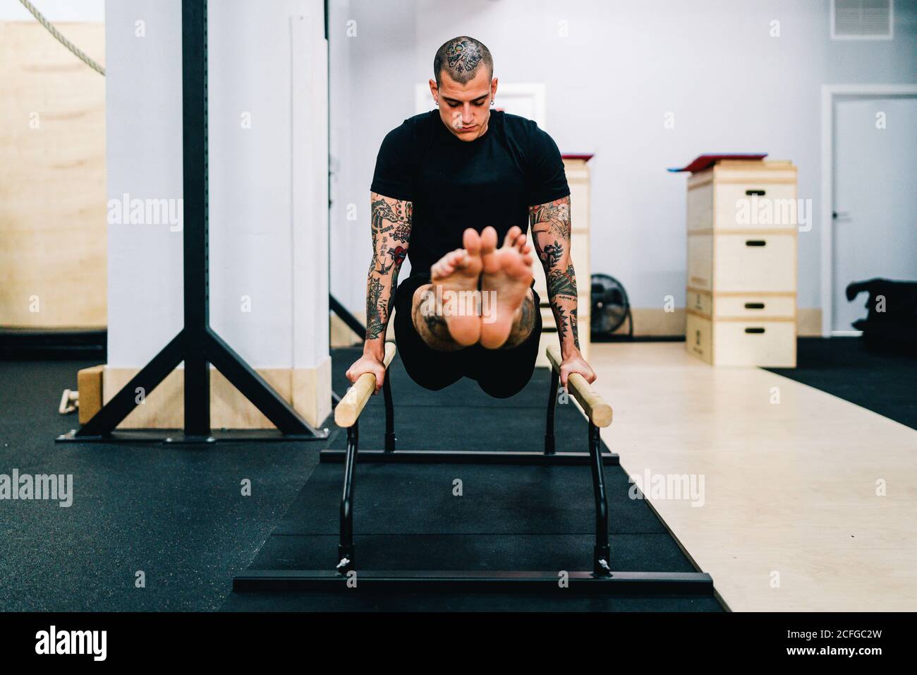 Tattooed strong male athlete doing abdominal exercises using parallel ...