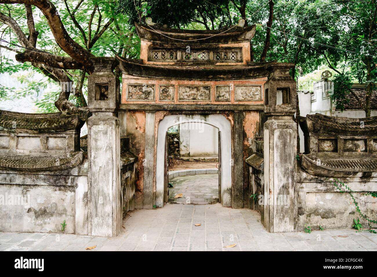 Exterior of stone arch entrance of old temple surrounded by tall trees ...