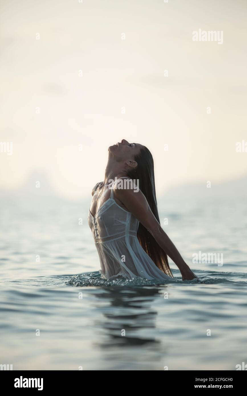 Sexy lady in translucent wet dress emerging from sea water in calm ...