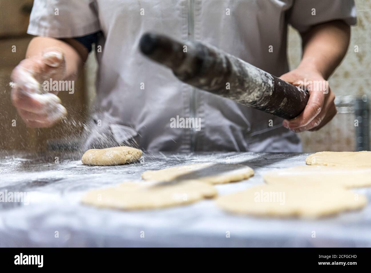 unrecognizable baker with rolling pin spilling flour on table while ...