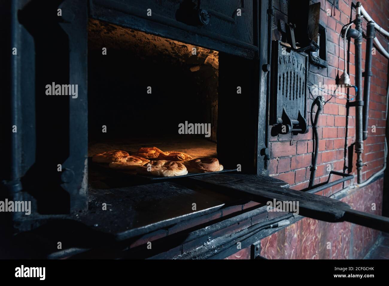 Set of fresh buns placed inside hot brick oven in professional bakery ...