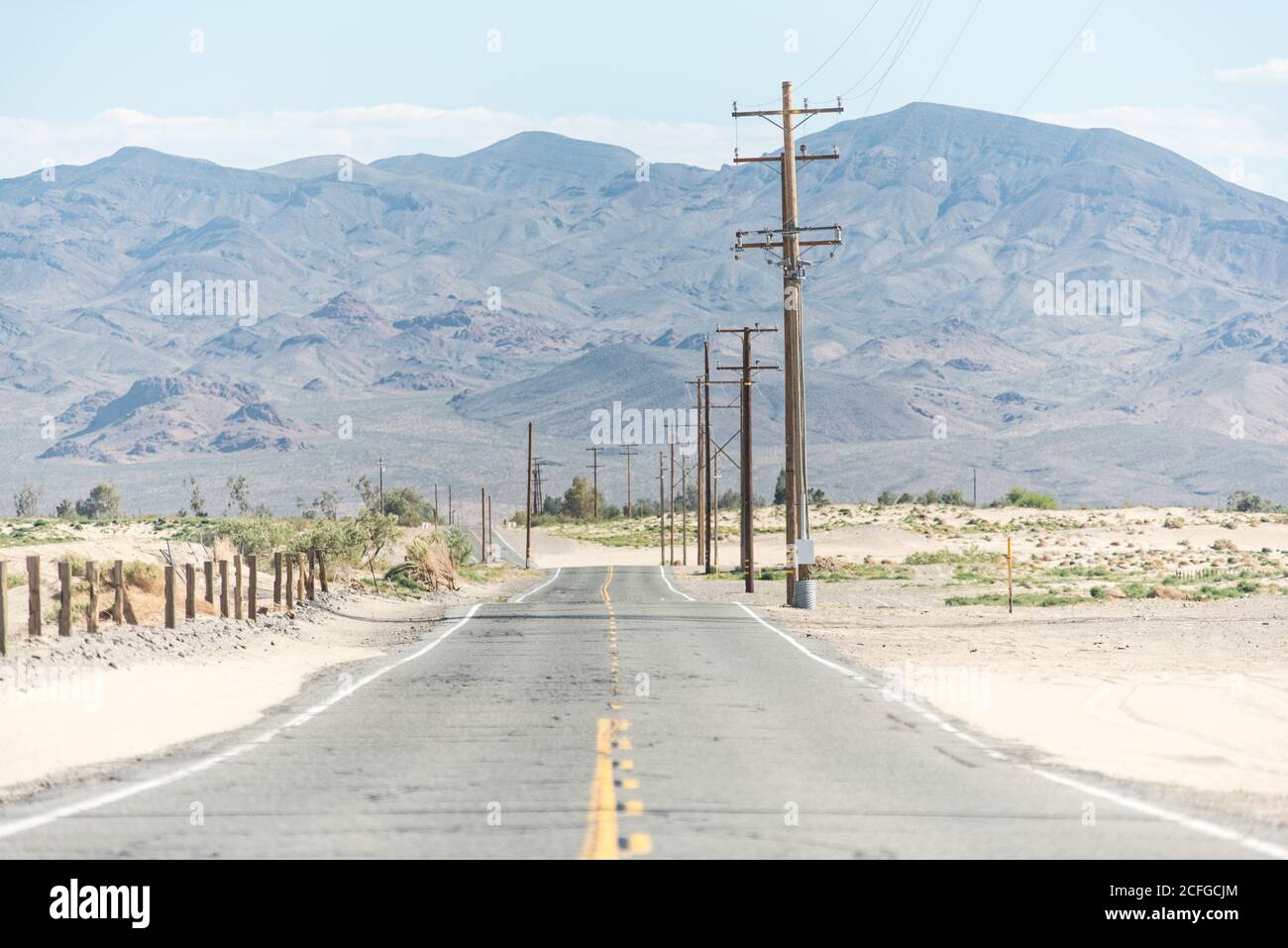 Rural highway at dusty field with power line and remote mountain range ...