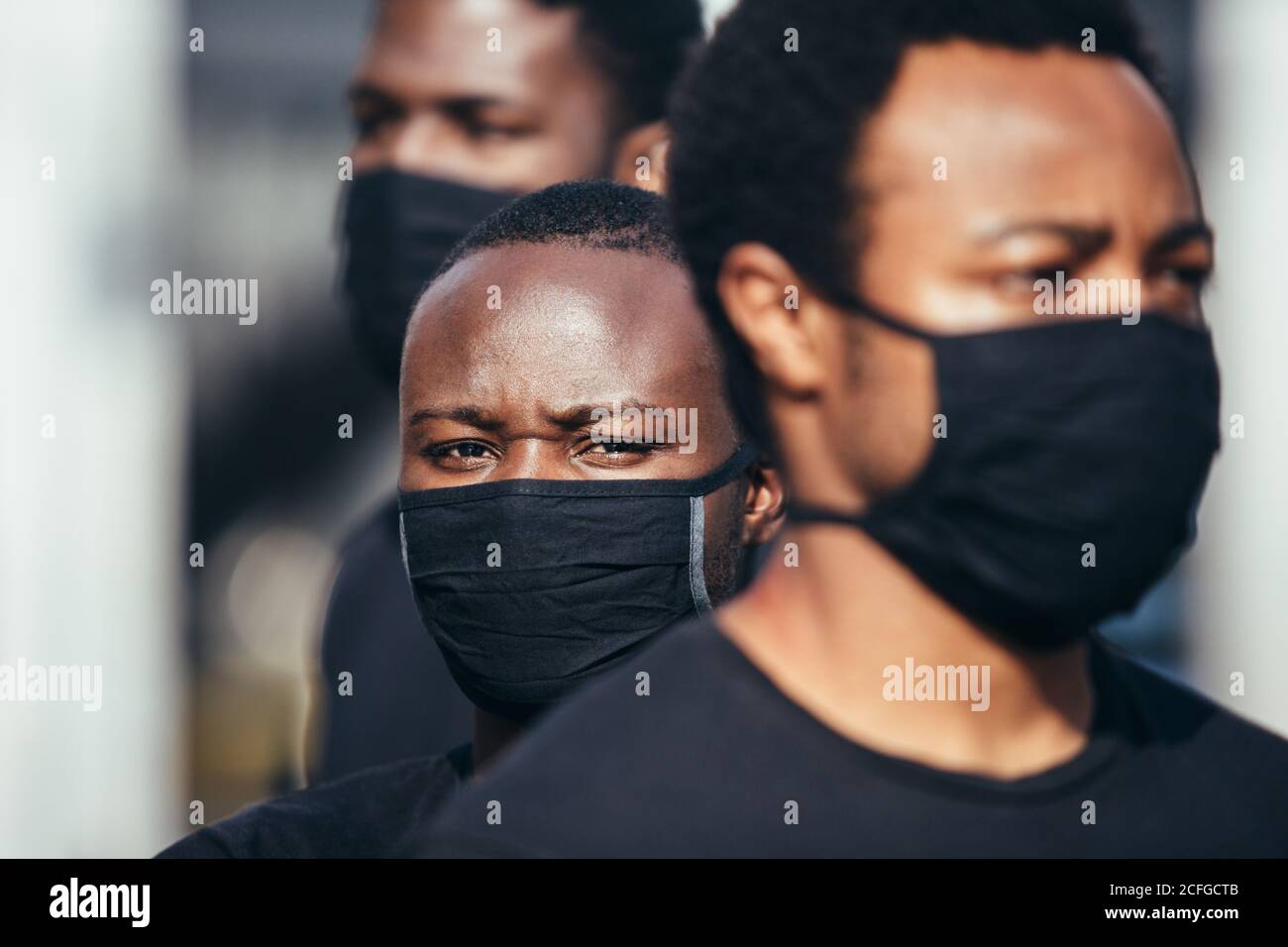Black men on street holding masks. One of the is looking at camera with ...