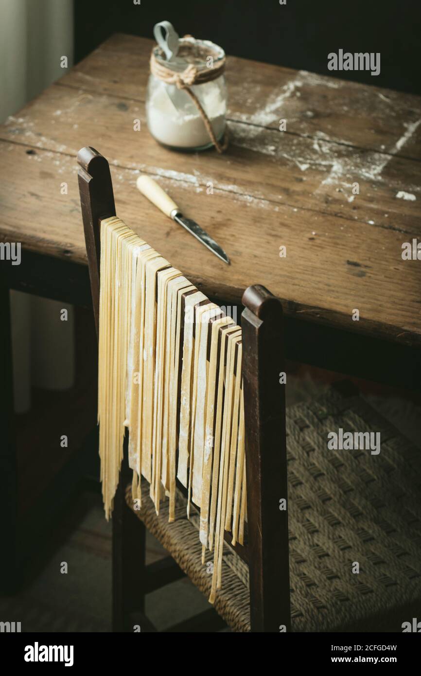 Fresh cooked pasta hanging on chair at kitchen table with flour on top ...