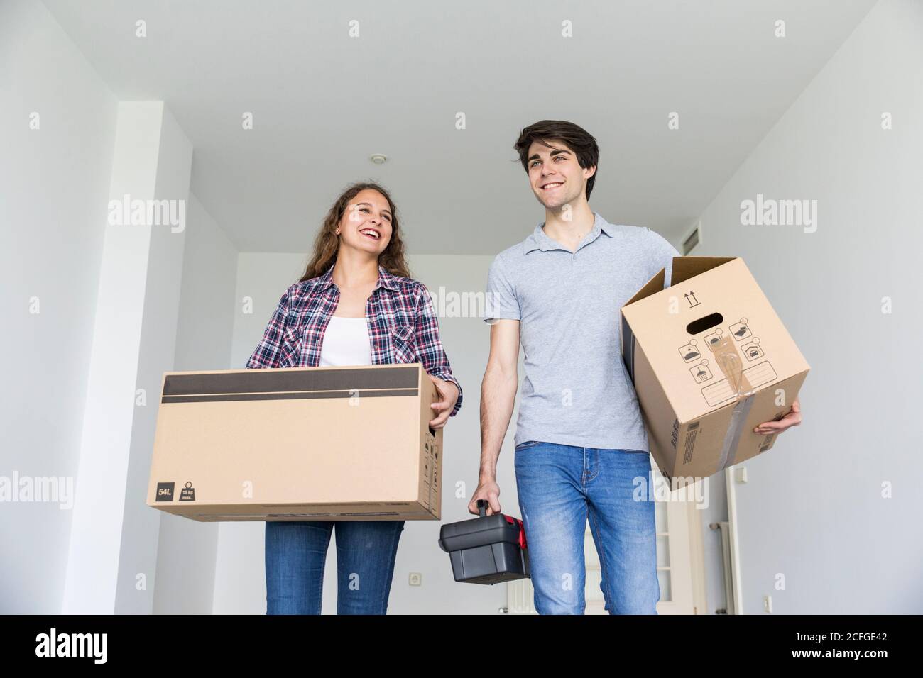 Young couple walking in empty room carrying carton boxes and tool bag ...