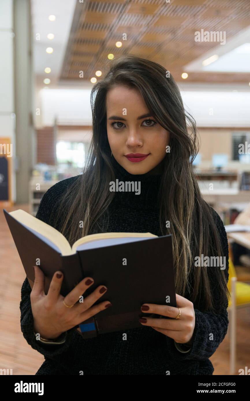 Pretty Woman standing along bookshelves and holding open book Stock ...