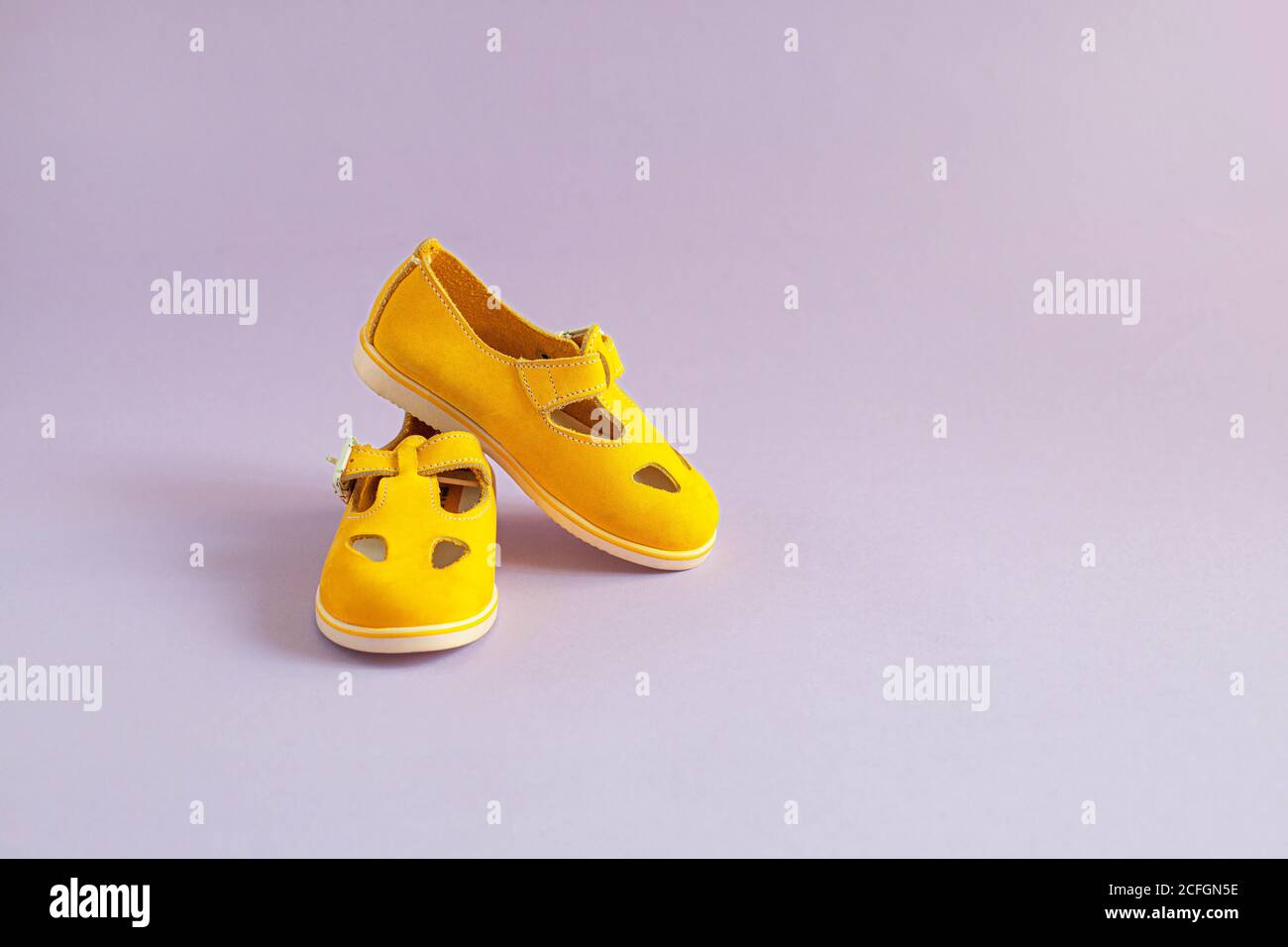 Bright yellow pair of shoes on lilac solid color background with a copy ...