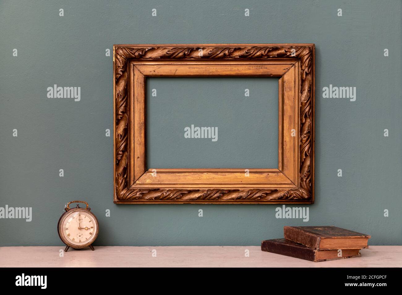 Empty gold vintage picture frame hanging on a green wall with clock and ...