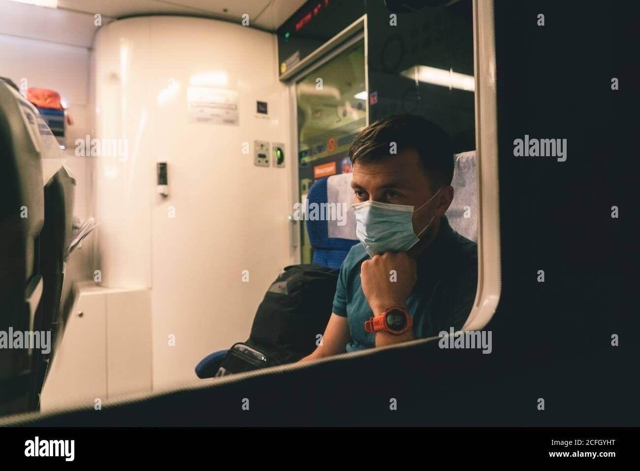 Tired and sad male passenger sits in face shield and looks through the ...