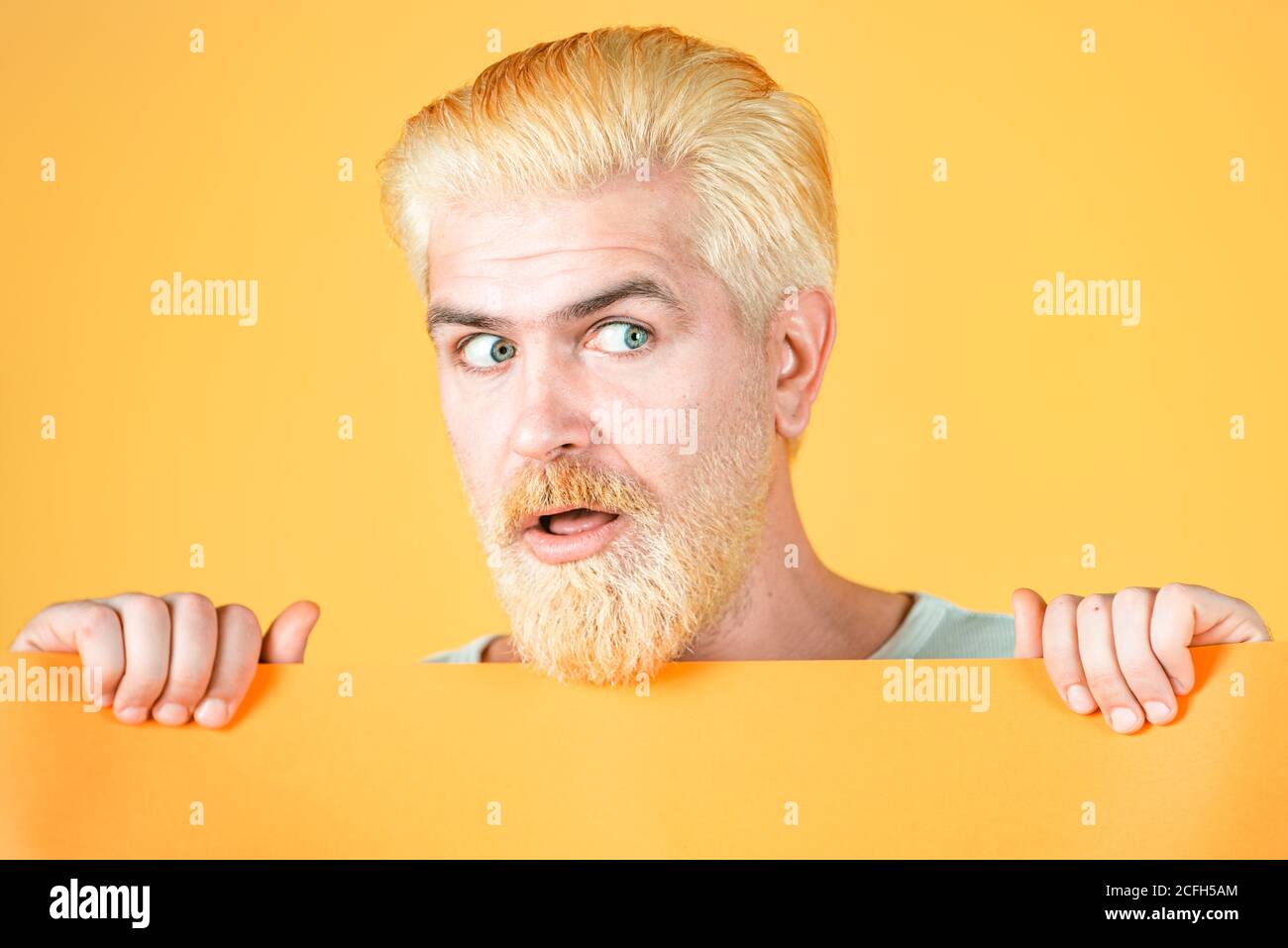 Funny man shows a sheet of paper in the camera on a yellow background ...
