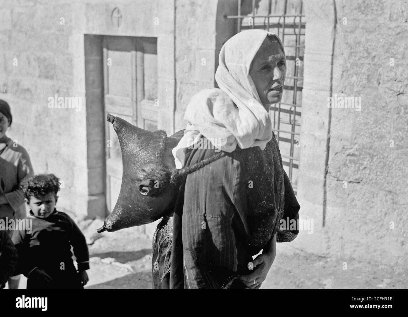 Original Caption: Bethlehem woman carrying water in a goatskin ...