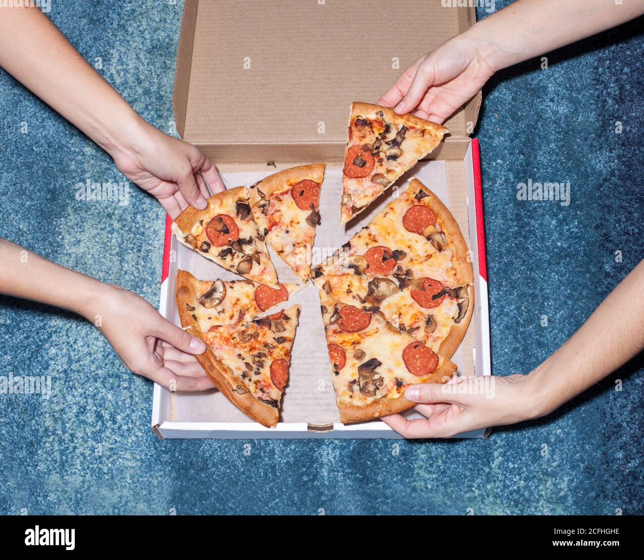 four hands take pizza pieces from pizza box on carpet at home, top view ...