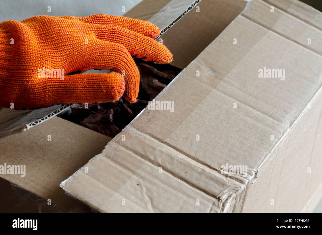 A worker wearing protective gloves opens a cardboard box. A hand with a ...