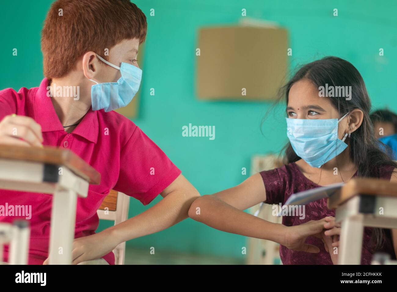 Two kid in medical mask at classroom greeting each other with elbow ...