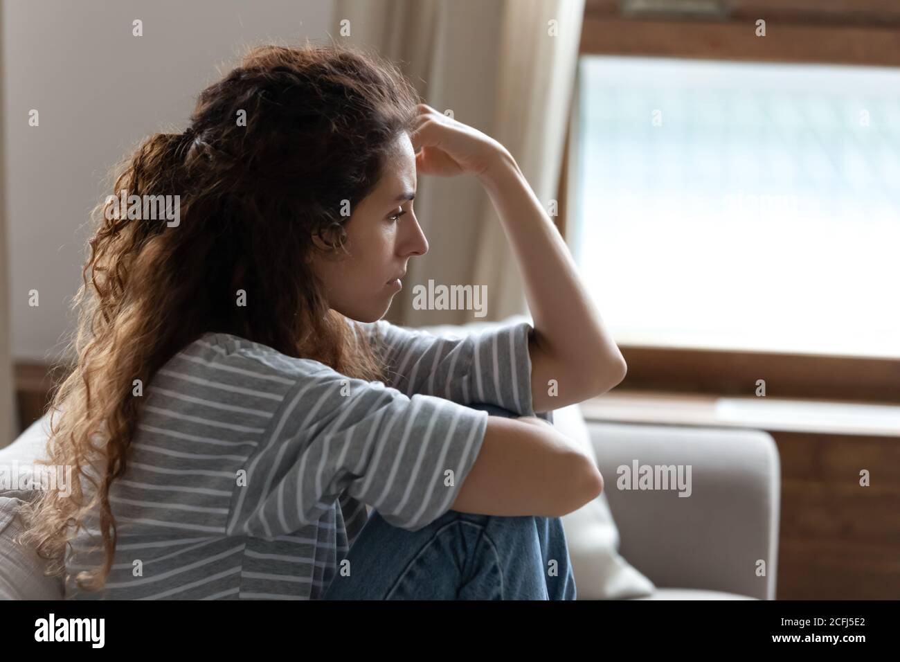 Sad young woman sitting on couch feels depressed side view Stock Photo ...