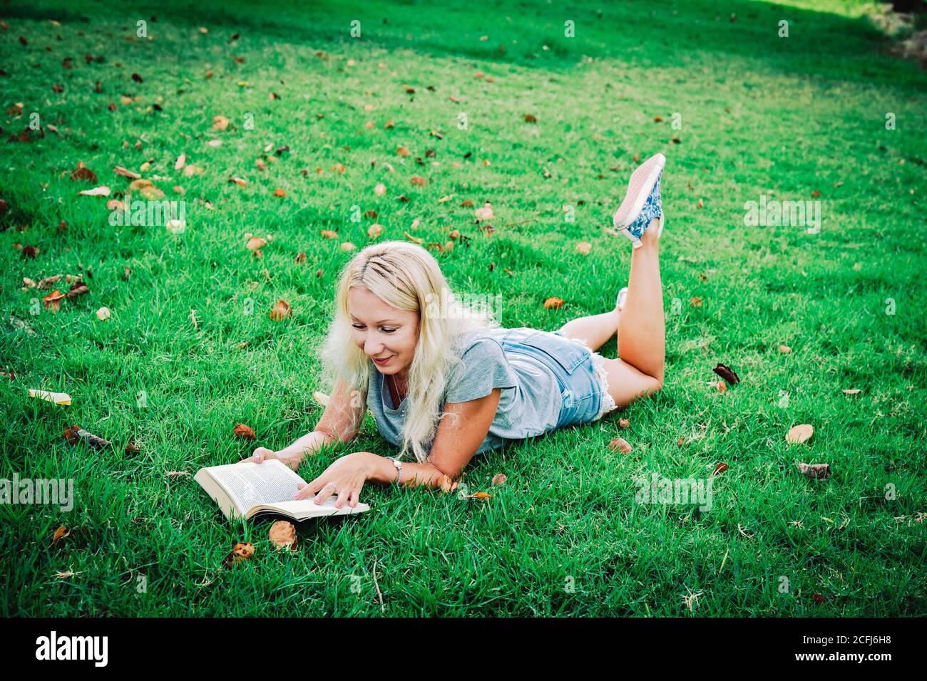 Smiling young woman reading a book lying on grass, photo with effect ...