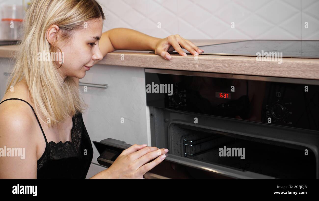Young woman cooking in the kitchen opening the oven door Stock Photo ...