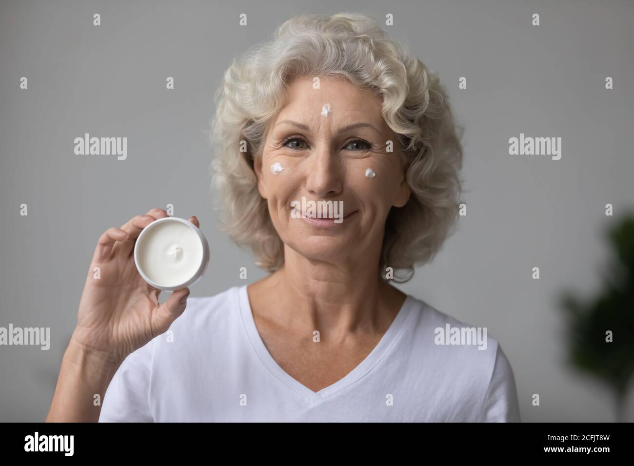 Head shot portrait satisfied mature woman holding moisturizing cream ...