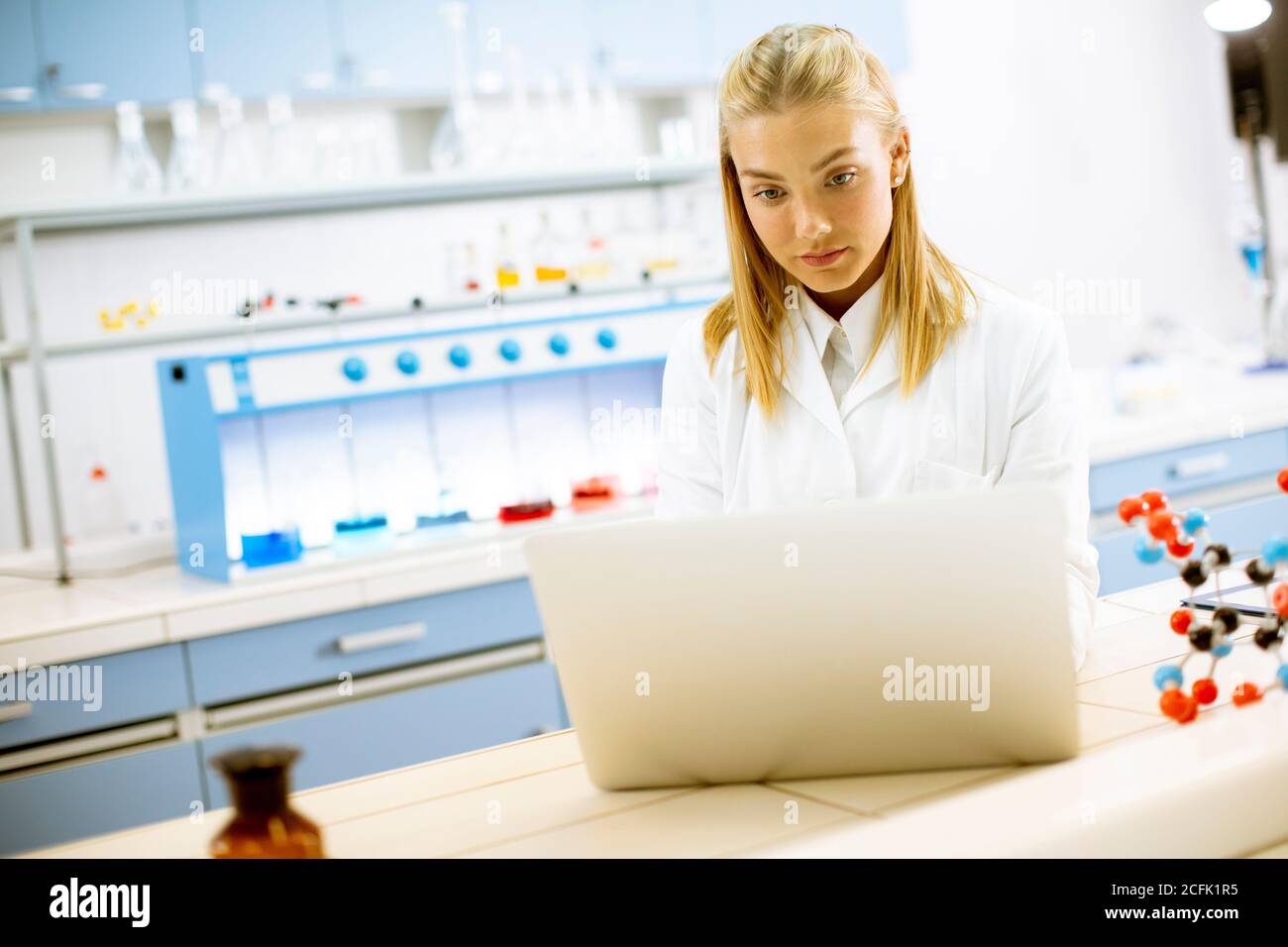 Cute female researcher in white lab coat using laptop while working in ...