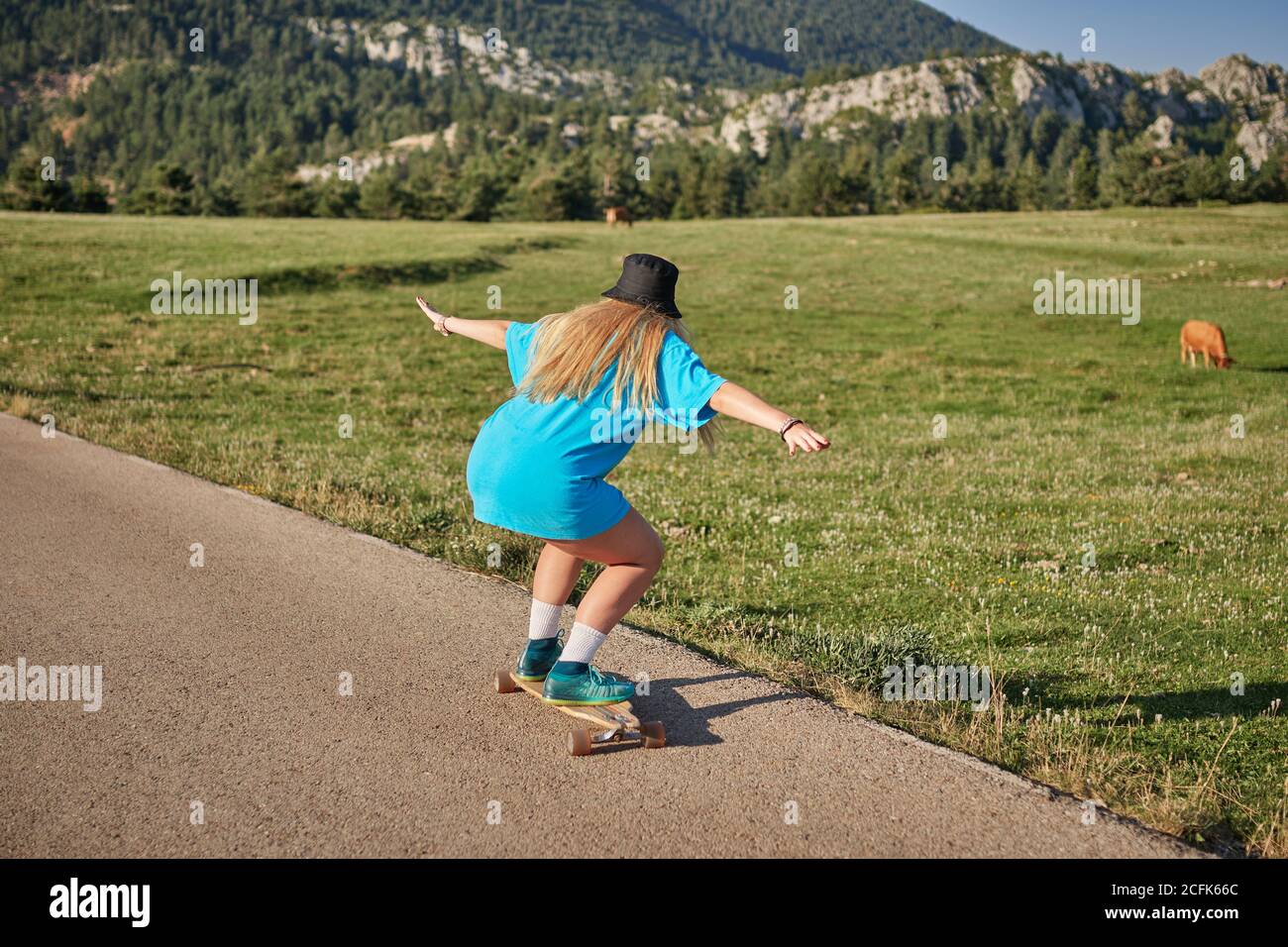 Back view of full body of focused female skater riding skateboard along ...