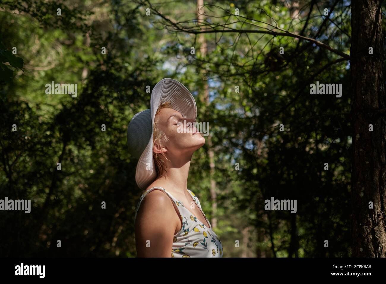 Side view of tranquil female standing in woods in summer and enjoying ...