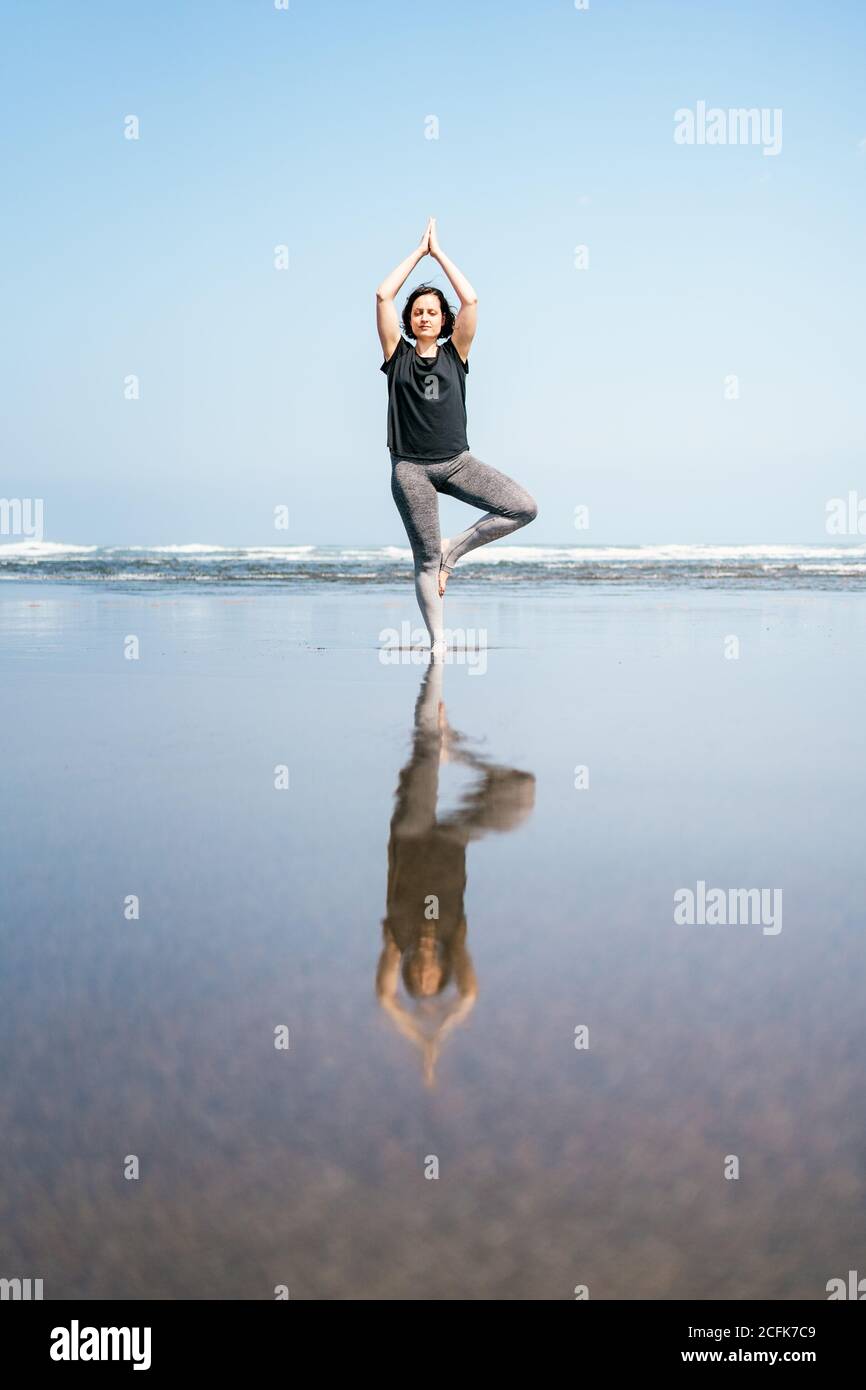 Full body young female in sportswear standing in Tree pose with arms up ...