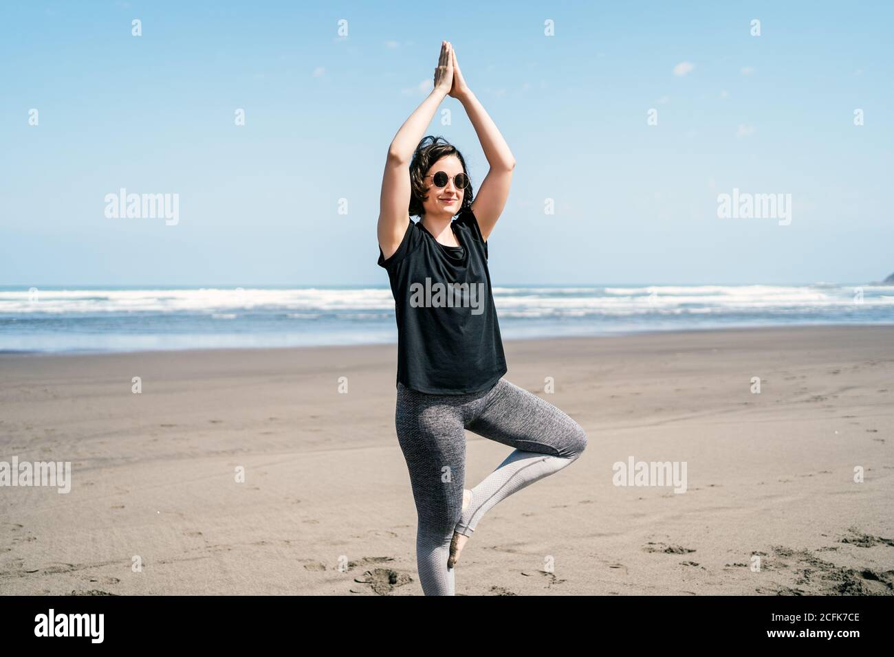 Full body young female in sportswear standing in Tree pose with arms up ...