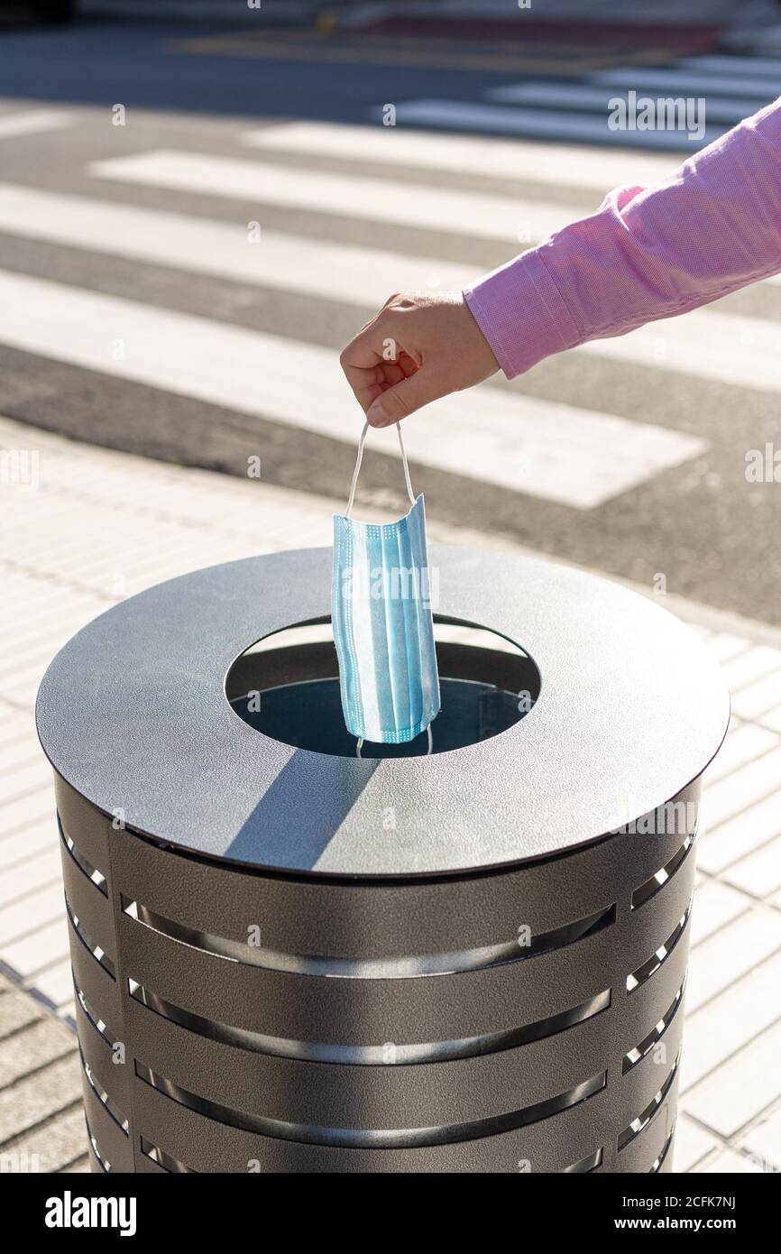 Female hand throwing out a face mask into the trash on the street ...