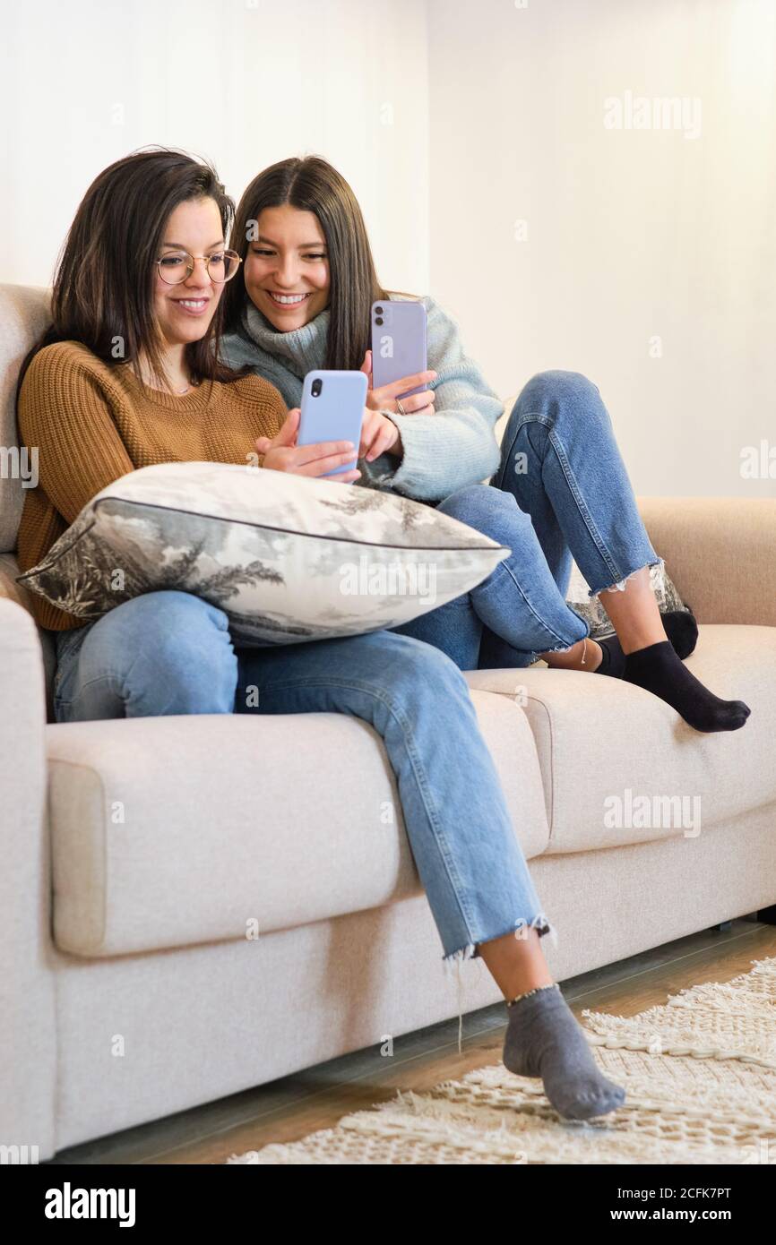 Positive female friends sitting on couch in cozy room and reading ...