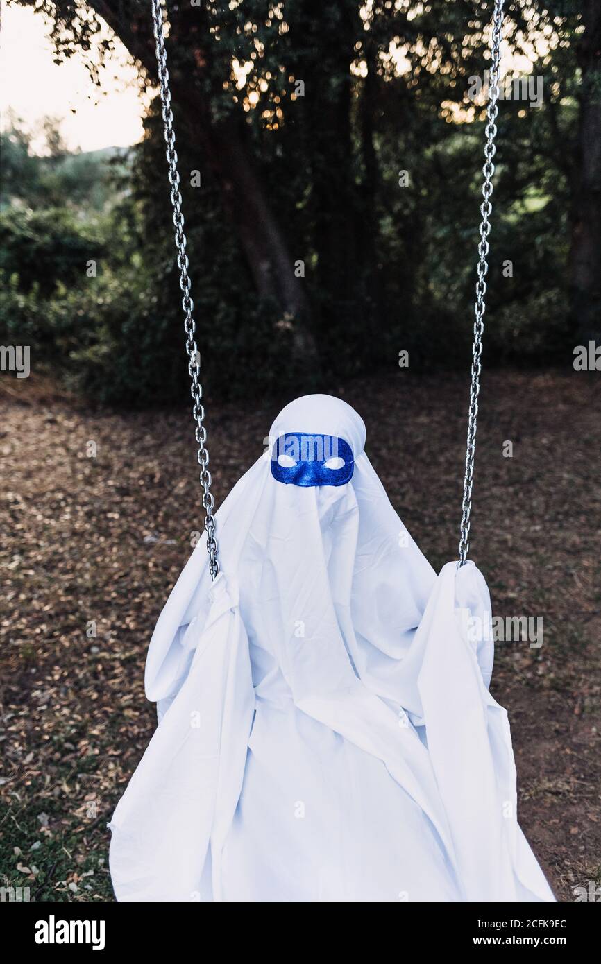 unrecognizable kid in white ghost costume swinging and playing on ...