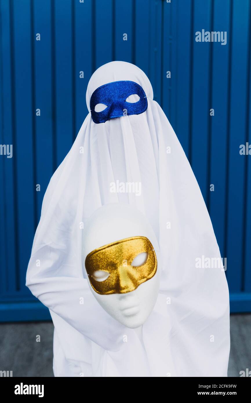 unrecognizable kid wearing masquerade mask and ghost costume standing ...