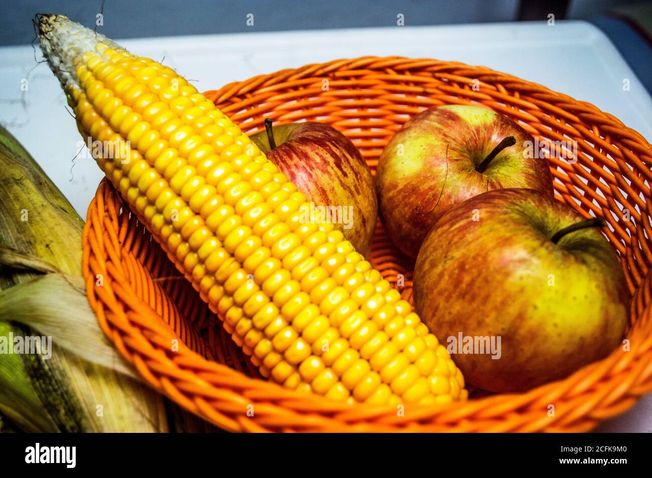 Raw sweet corn and apple arrange in a plastic wired bascket on blurred ...
