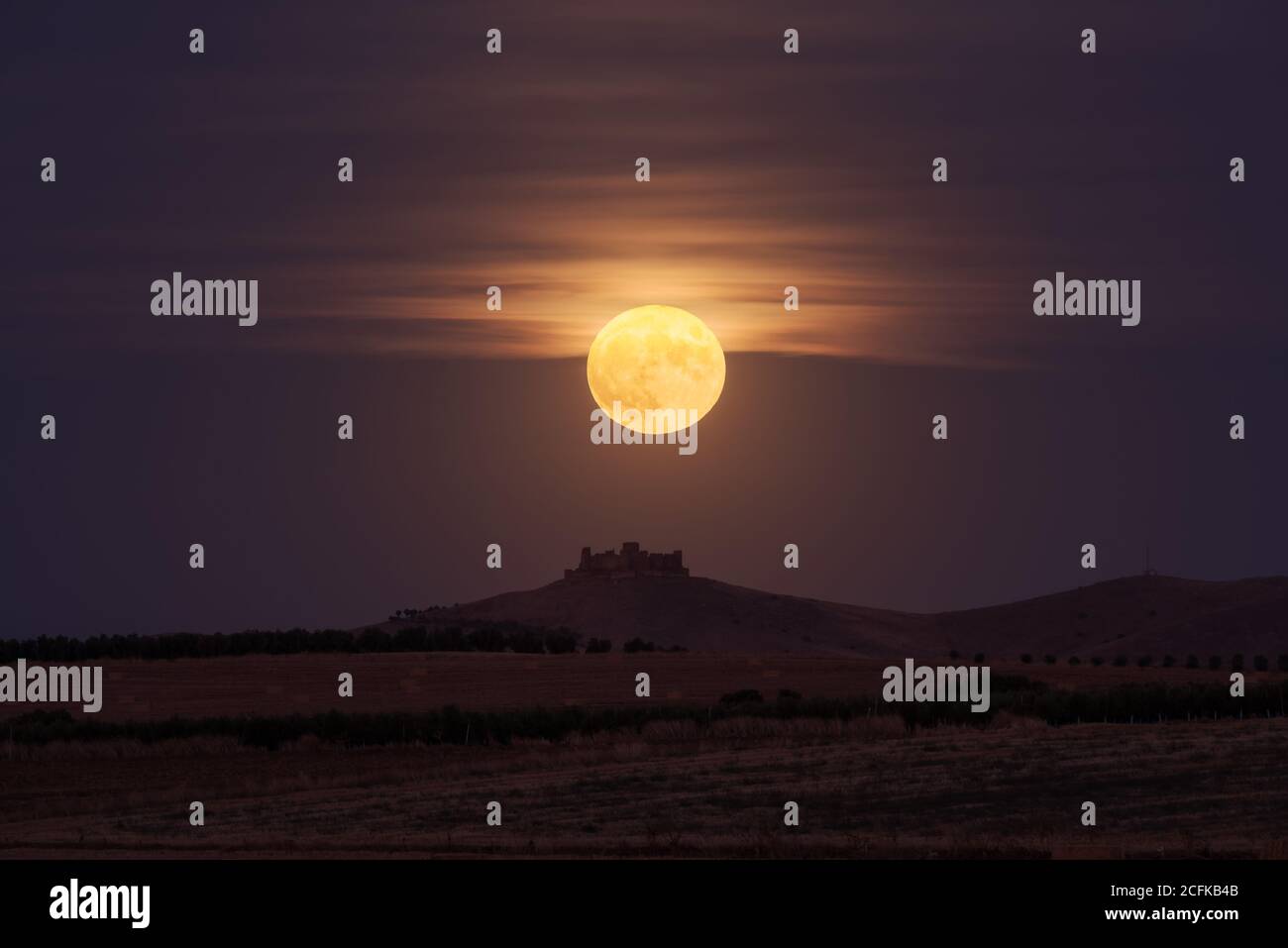 Bright yellow moon glowing on night sky over distant castle and fields ...