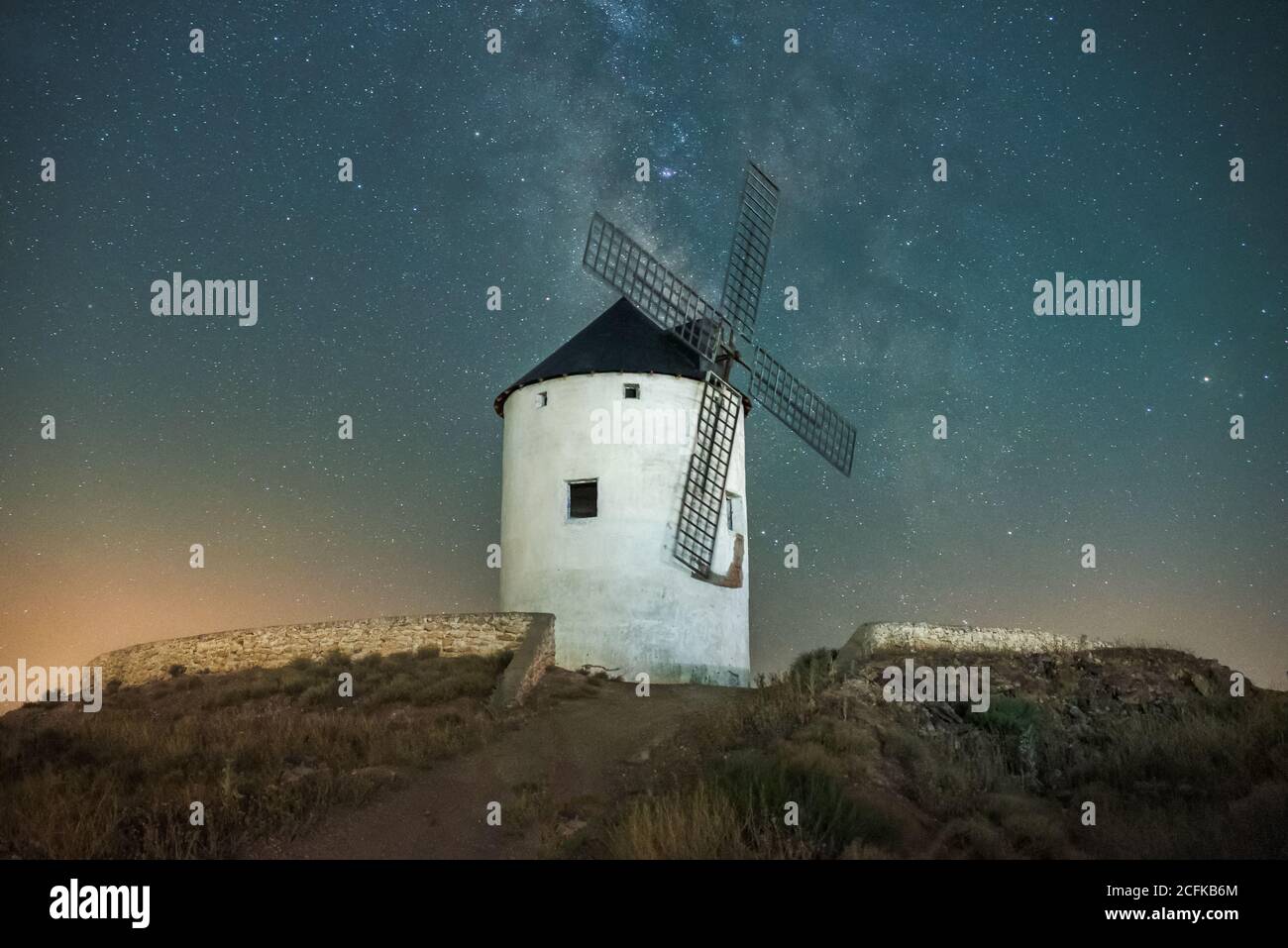 Low angle of old white windmill tower located on hill against starry night sky with Milky Way ...