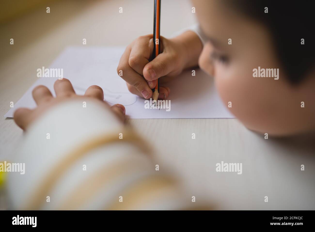 Side view of crop cute kid sitting at wooden table and drawing with ...