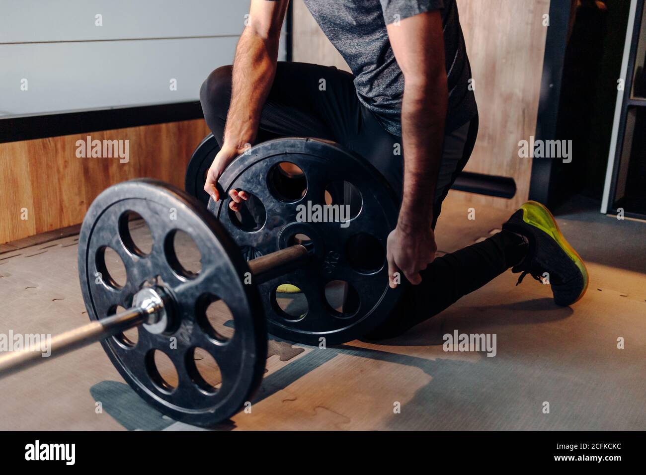 Crop anonymous male athlete in sportswear putting heavy plates on ...