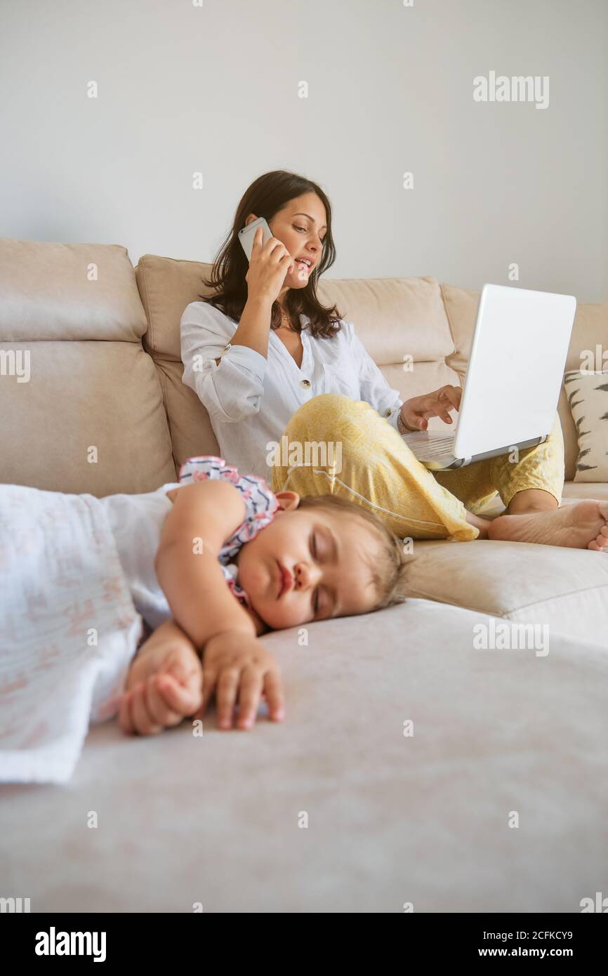 Little girl sleeping on the sofa while her mother works with a laptop ...