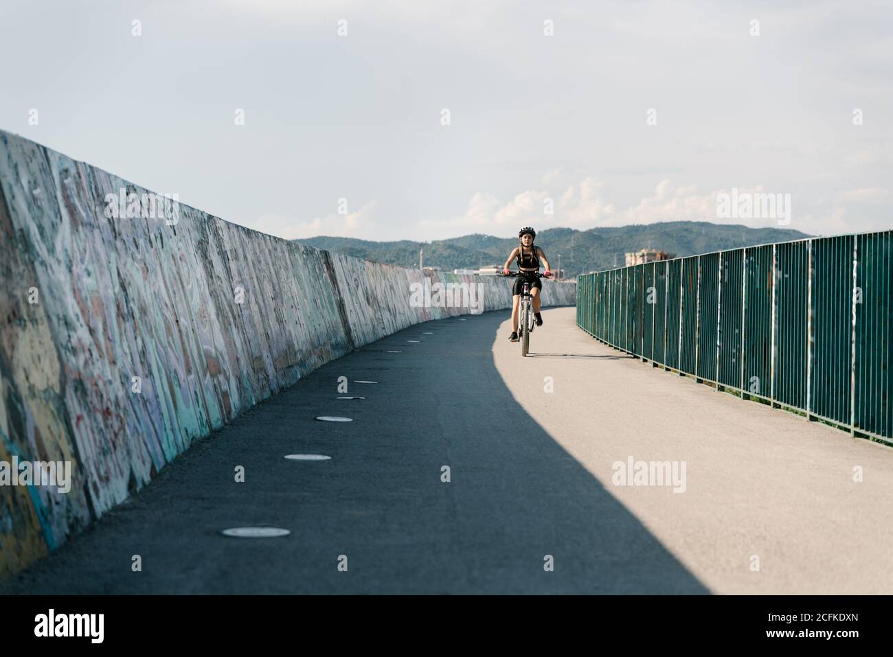 Low angle of confident young female bicyclist in sportswear and helmet ...