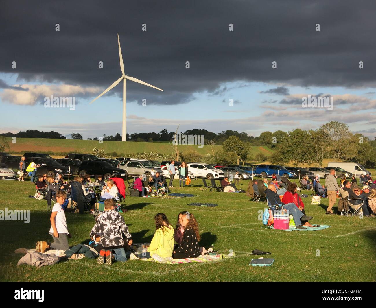 Picnickers in a field with cars parked in the background for an outdoor ...