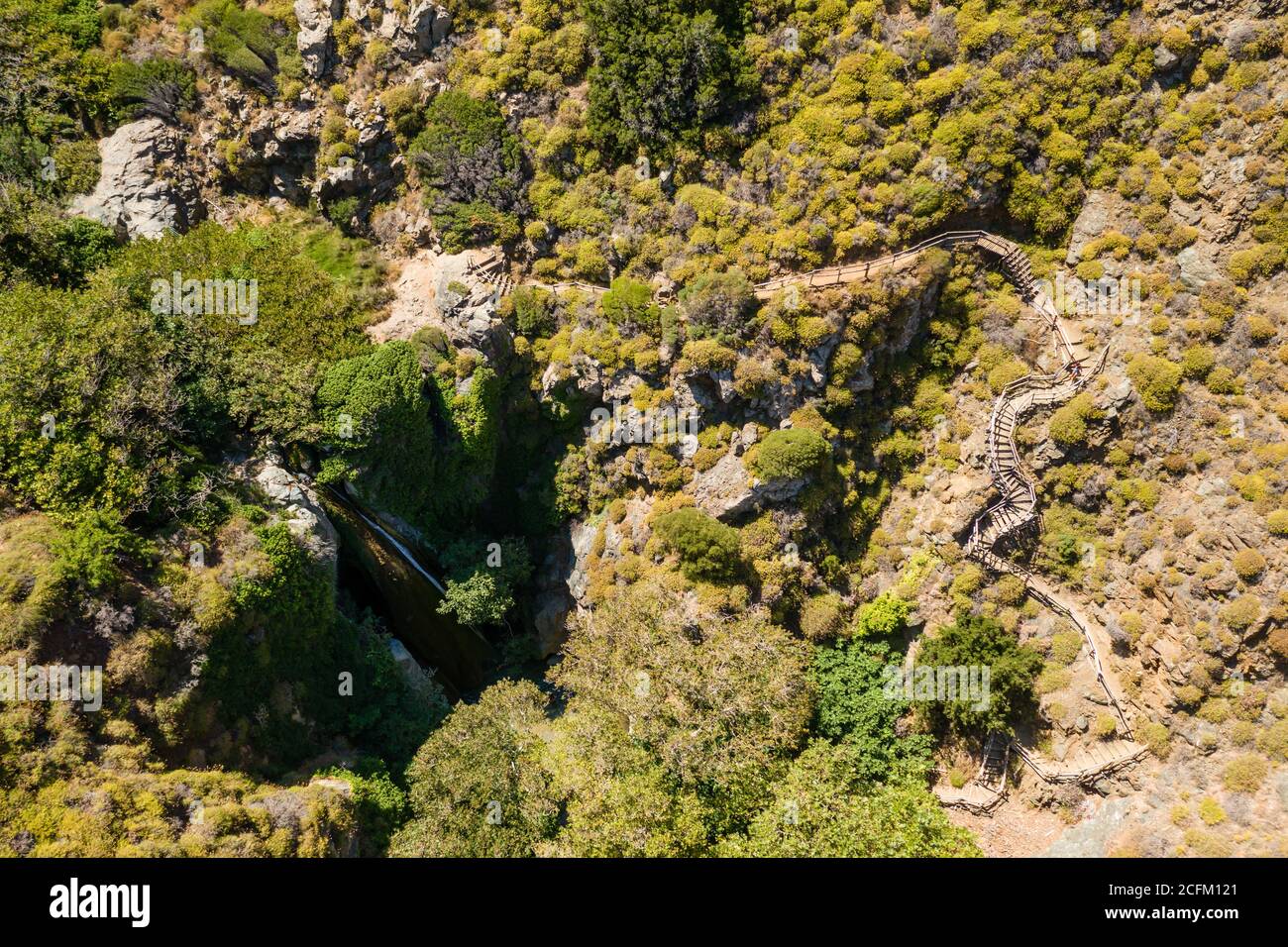 Aerial view of a waterfall in a narrow gorge next to winding wooden ...