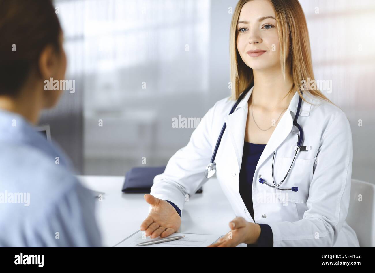 Unknown woman-doctor is writing some medical recommendations to her patient, while they are ...