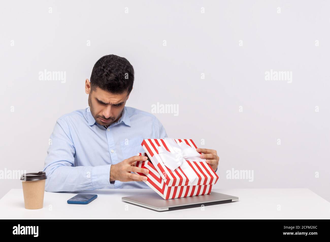 Curious man employee sitting in office workplace, opening gift box and ...